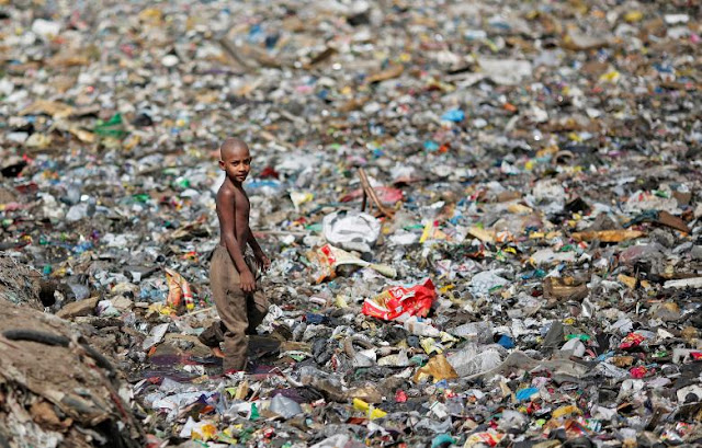 A boy walks on a pile of garbage covering a drain in New Delhi